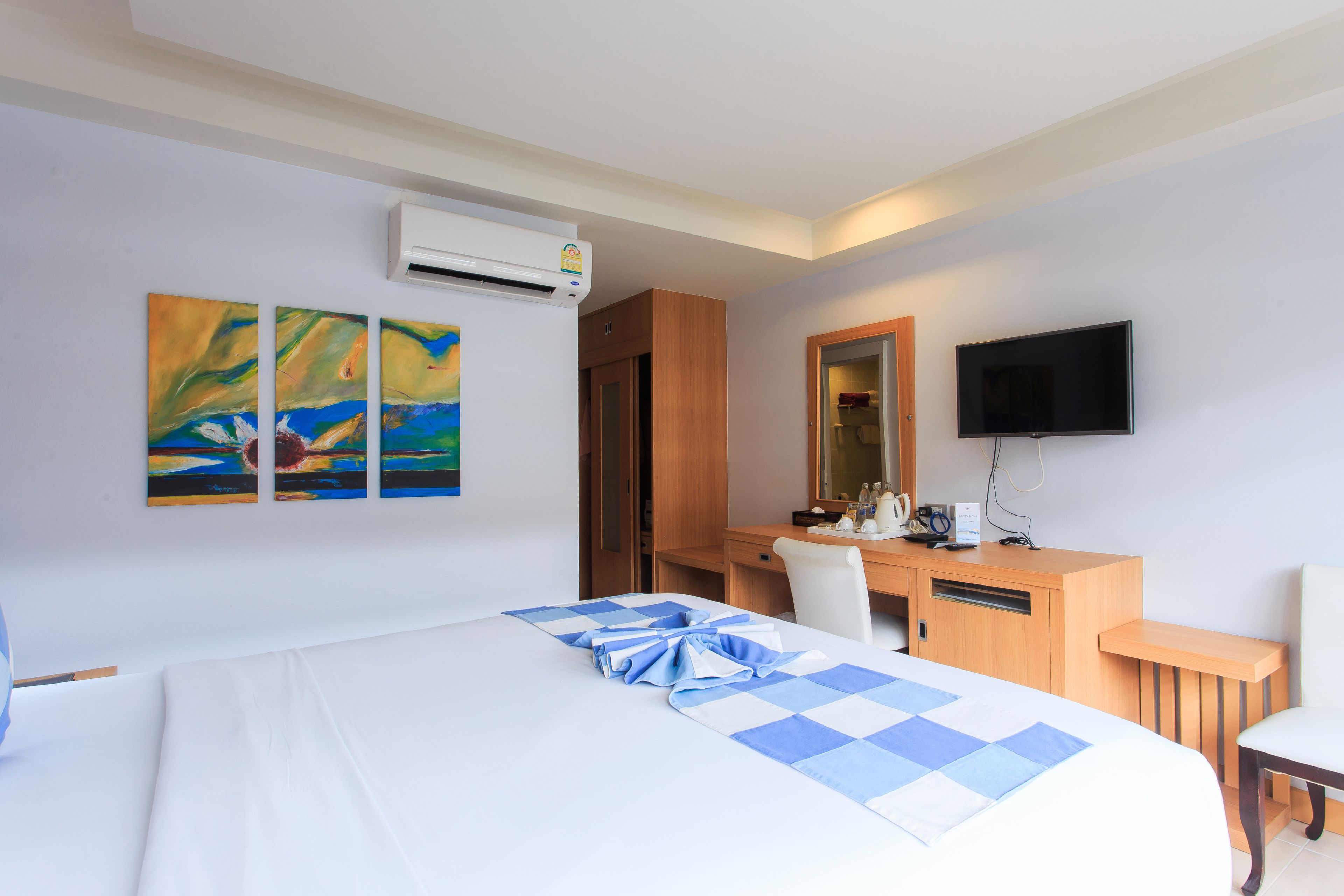 Quarto de hotel com cama, escrivaninha, cadeira, televisão e obras de arte na parede.
