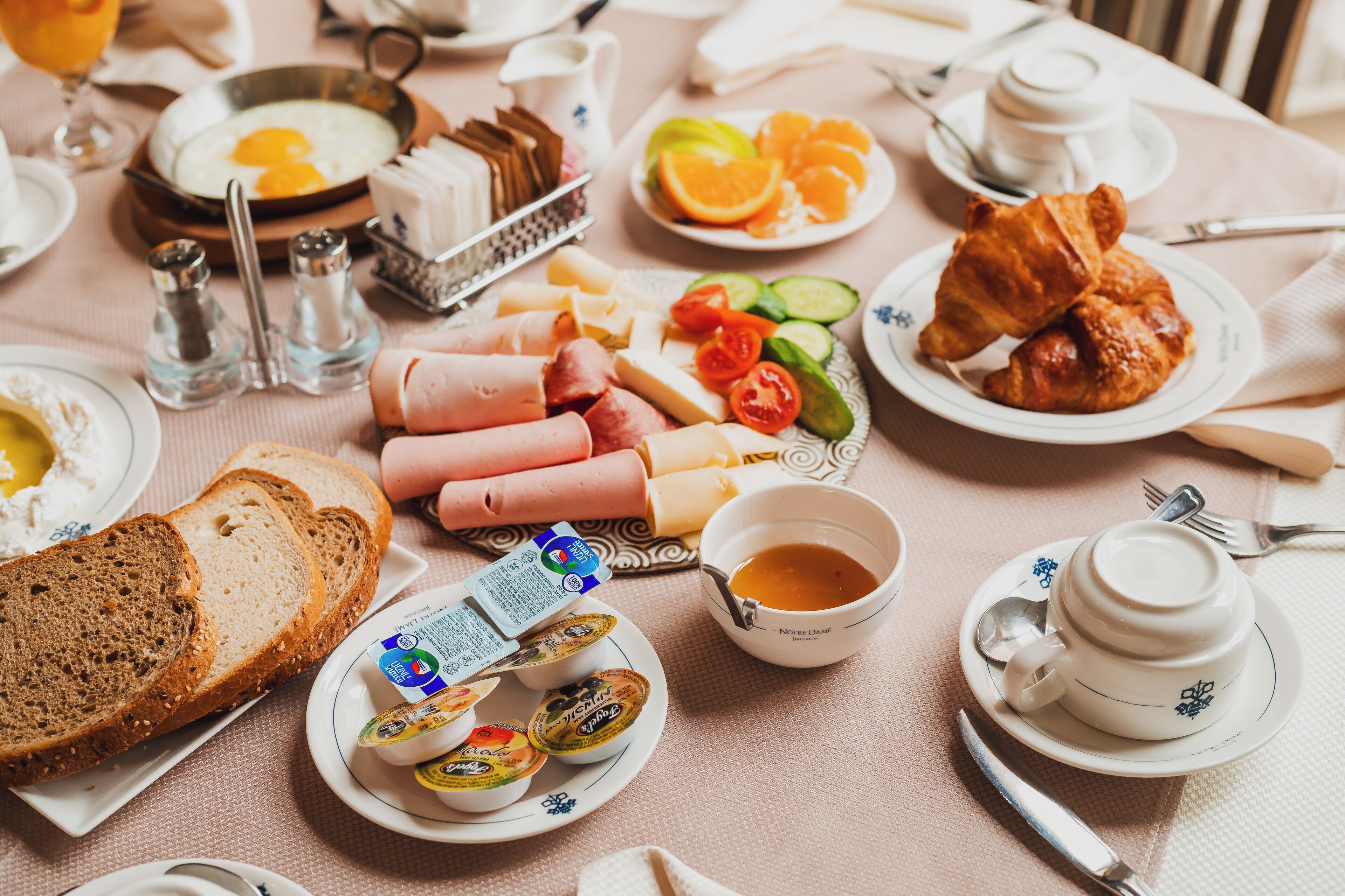 Uma mesa de café da manhã com diversos alimentos, como ovos, pão, queijo e frutas.