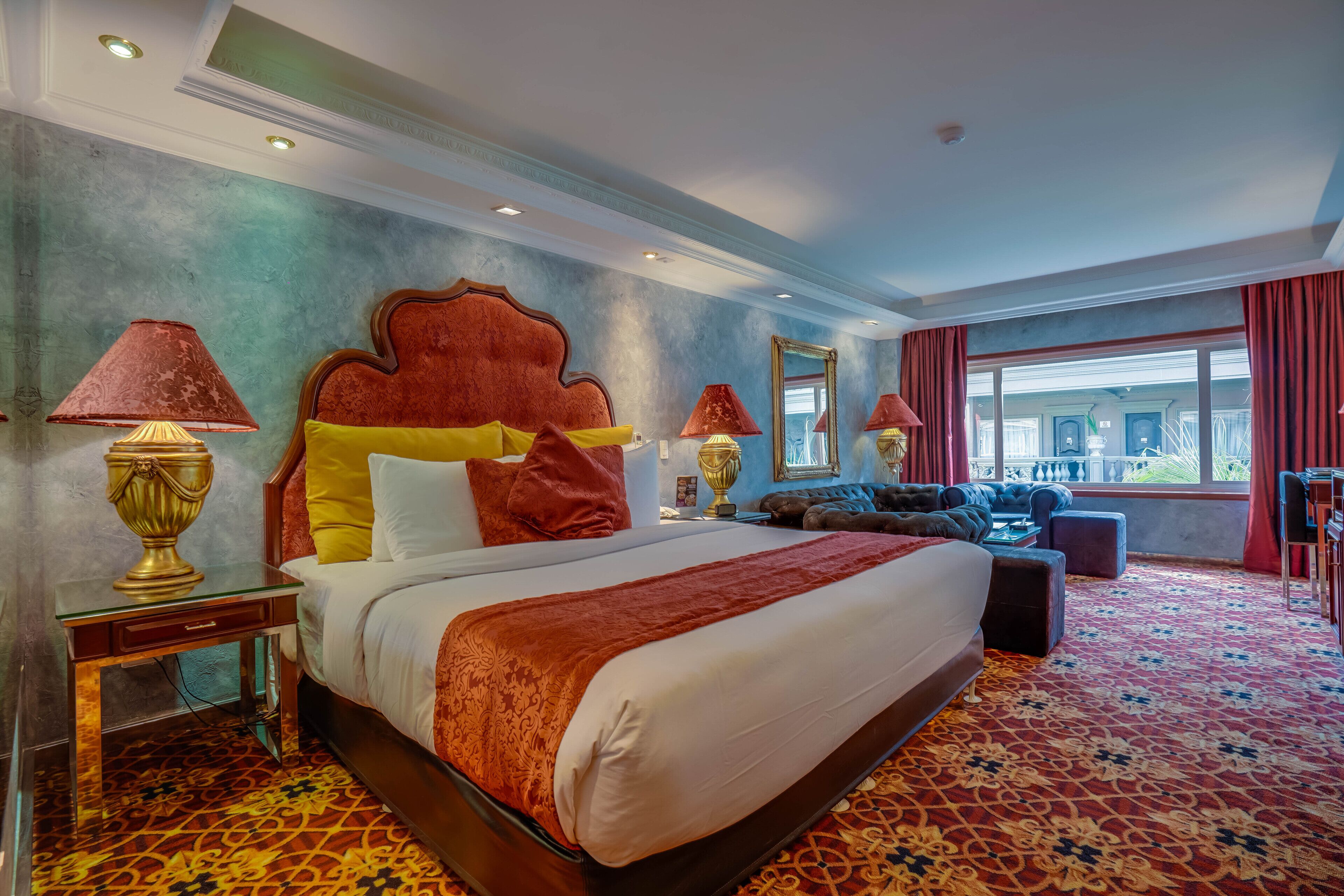 Quarto de hotel com uma cama grande, um sofá, uma mesinha e uma janela com cortinas.