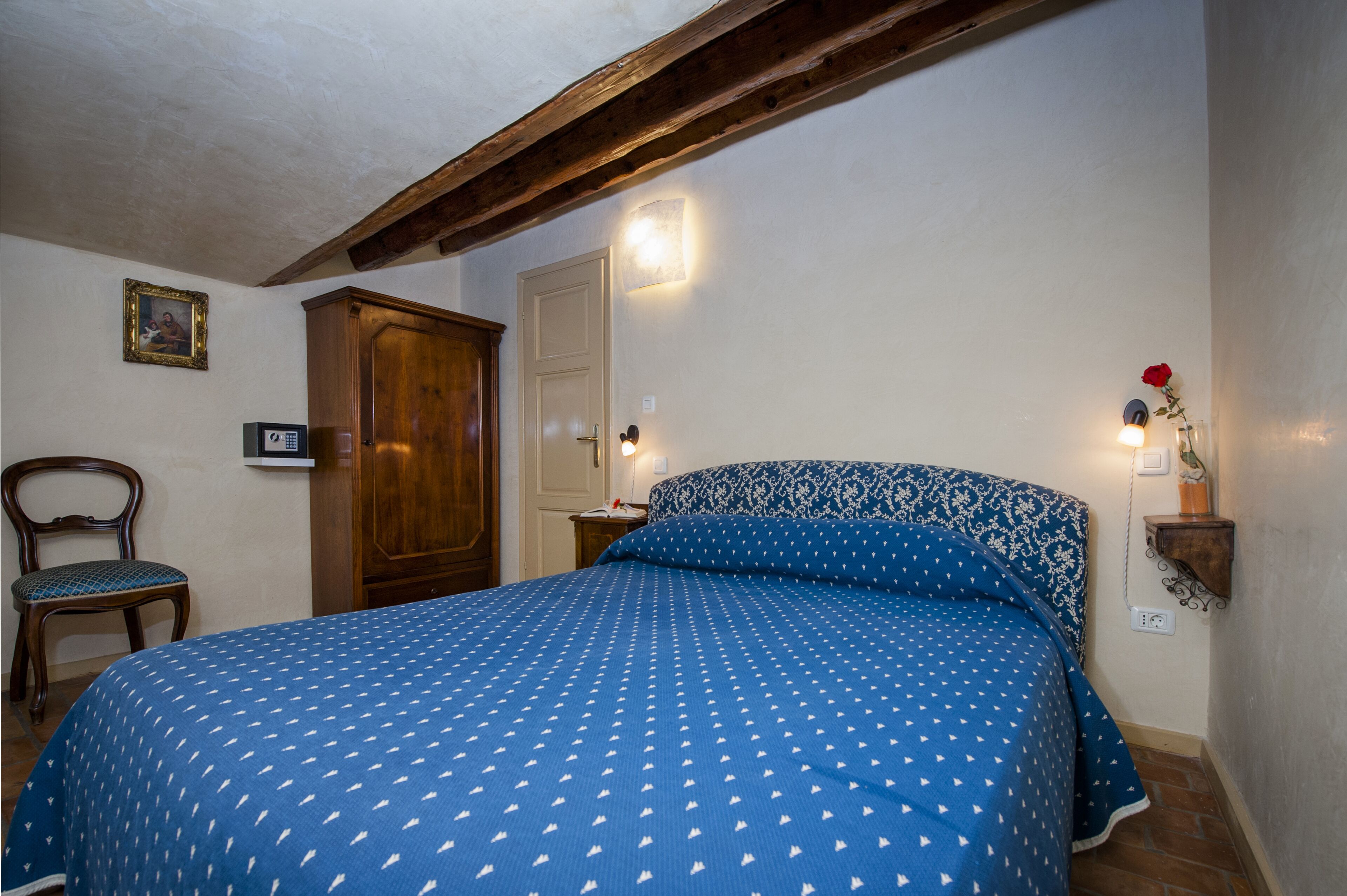 Quarto com cama, cadeira de madeira, guarda-roupa e luminárias fixadas na parede.