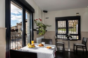 Uma sala de jantar com mesa posta para o café da manhã, uma planta em vaso e vista para um castelo através de grandes janelas.
