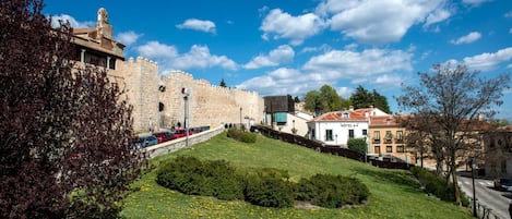 Um edifício de pedra histórico com uma rampa de acesso, rodeado por vegetação e edifícios modernos.