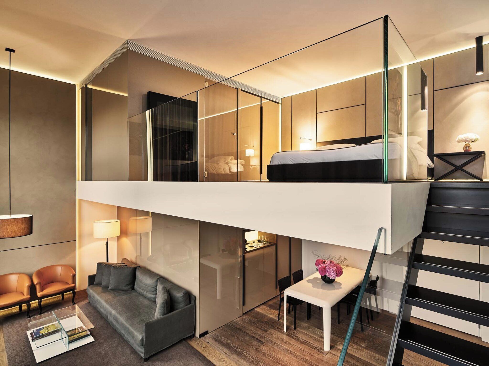 Quarto de hotel moderno com cama mezanina, um sofá, uma pequena mesa com flores e uma escada.