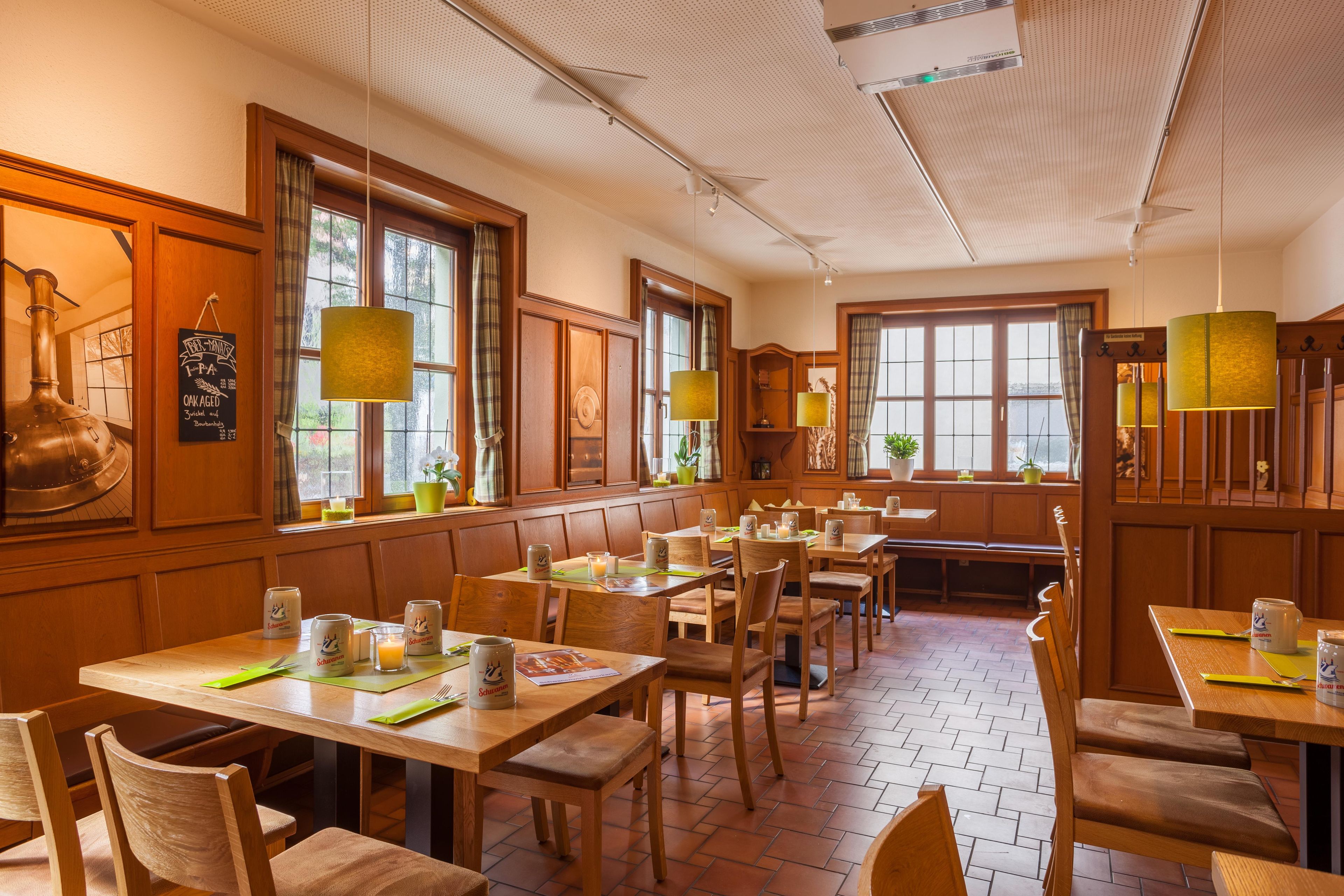 Restaurante com mobiliário de madeira, janelas amplas e luminárias pendentes.