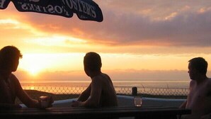 Três pessoas sentadas à mesa com vista para o pôr do sol sobre o oceano.