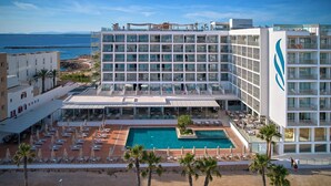 Um hotel com piscina no terraço, várias varandas e vista para o mar.