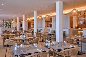 Um restaurante moderno com várias mesas e cadeiras, luminárias pendentes grandes e um espaço de bar.