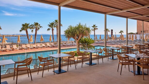 Área à beira da piscina com espreguiçadeiras e guarda-sóis, com vista para a piscina e o oceano.