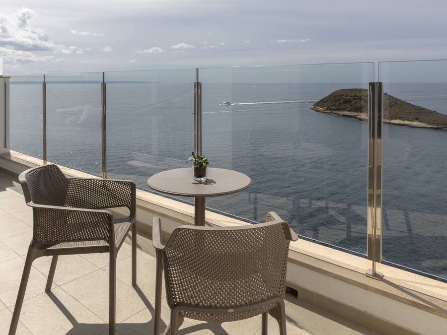 Varanda com duas cadeiras de vime e uma mesa redonda pequena, com vista para um corpo d'água e uma ilha ao longe.