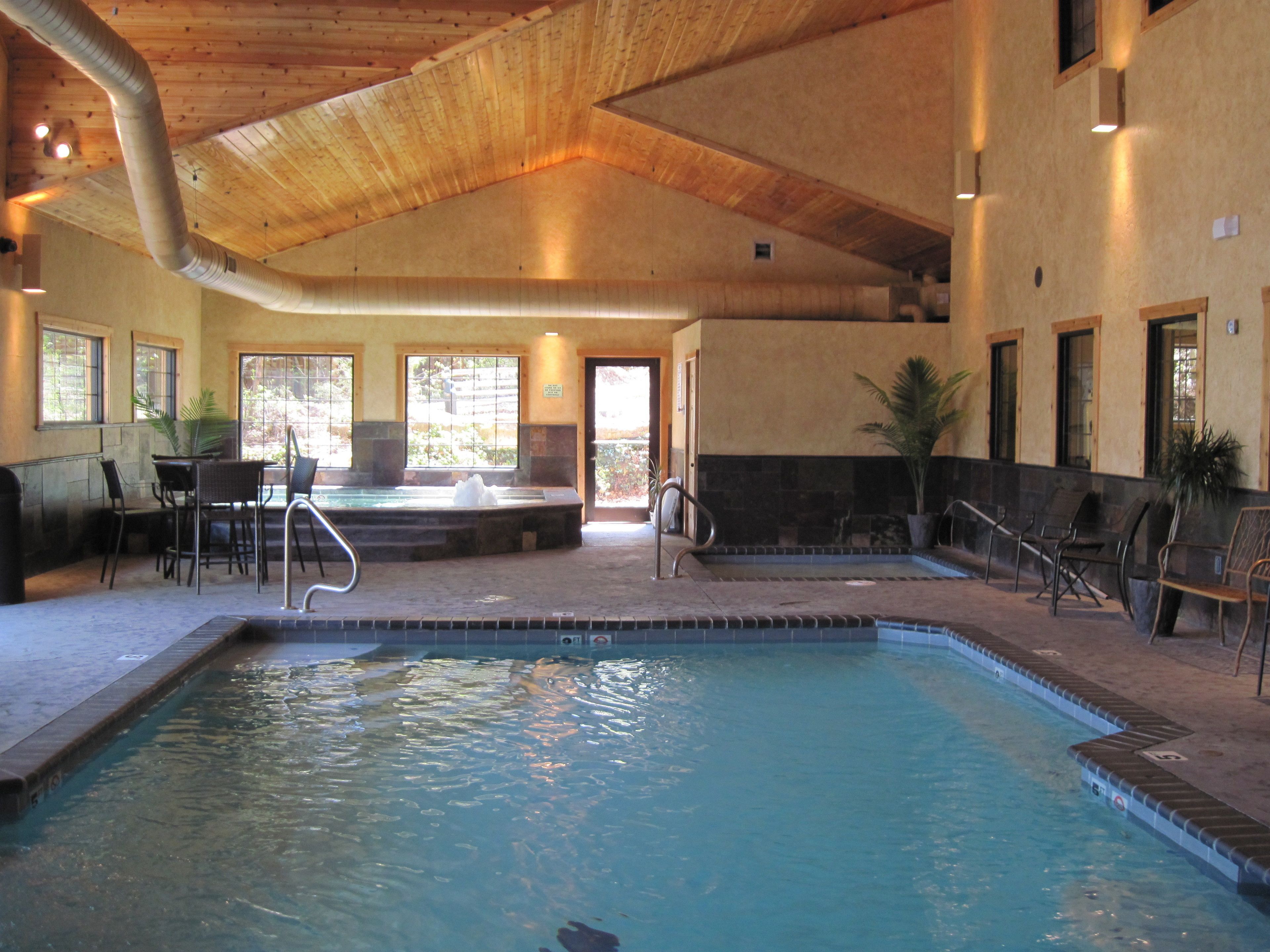 Piscina interna com teto de madeira, área de estar e ofurô.