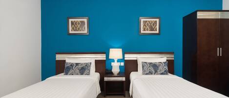 Quarto de hotel com duas camas, uma mesa de cabeceira com luminária e um guarda-roupa.