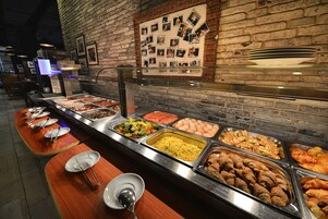 Um buffet com diversas opções de comida, uma parede de tijolos e uma exposição de fotografias.