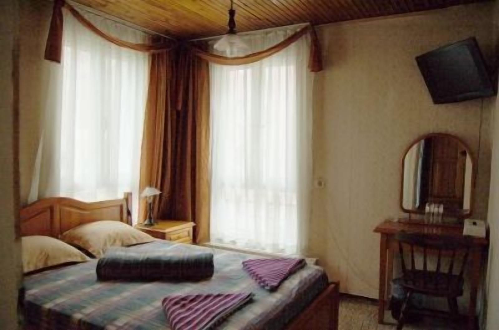 Um quarto com uma cama, uma cadeira, uma escrivaninha, um espelho e uma televisão.