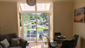 Quarto com sofá, mesa de jantar, cadeiras e vista para barcos estacionados através de uma porta de vidro.