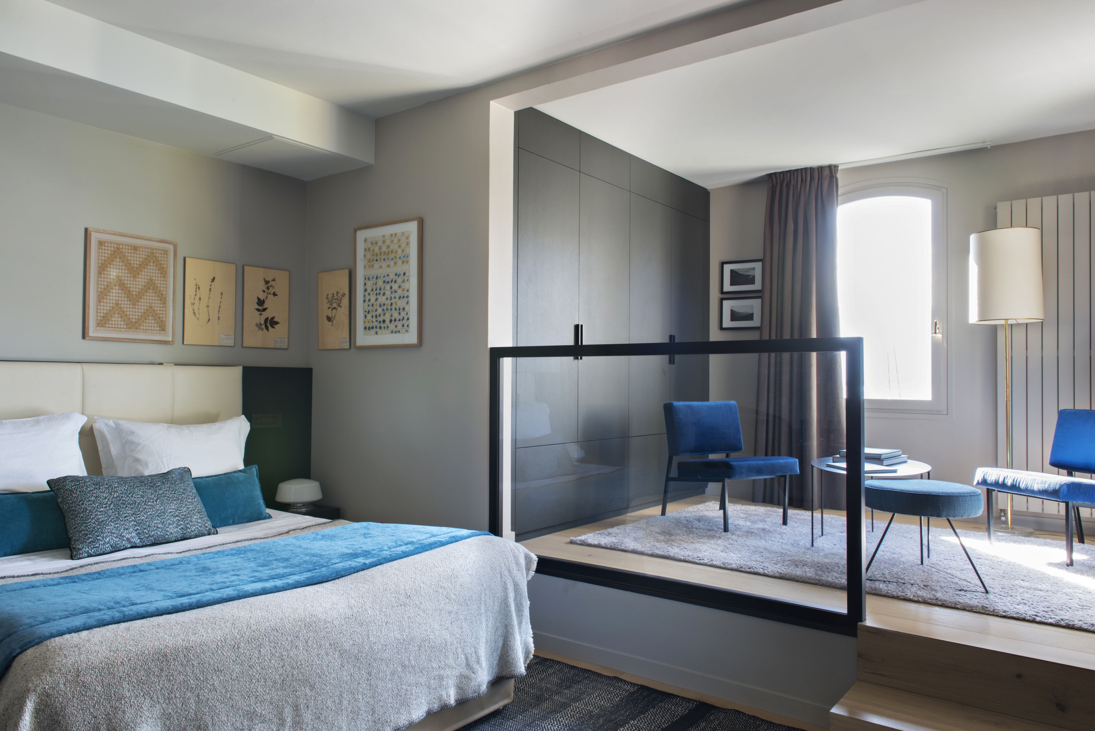 Quarto de hotel moderno com uma cama grande, área de estar com cadeiras e obras de arte nas paredes.