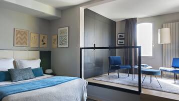 Quarto de hotel moderno com uma cama grande, área de estar com cadeiras e obras de arte nas paredes.