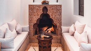 Uma sala de estar acolhedora com lareira, dois sofás brancos e uma pequena mesa de madeira com uma vela.