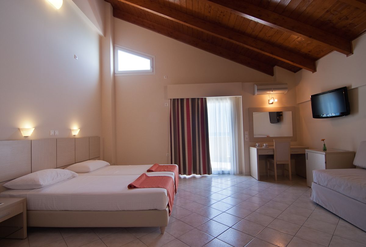 Quarto de hotel com duas camas, uma mesa, televisão e chuveiro.