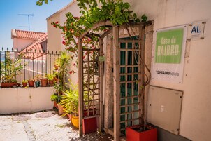 Um pátio com pérgola de madeira, plantas em vasos e uma placa com a inscrição 