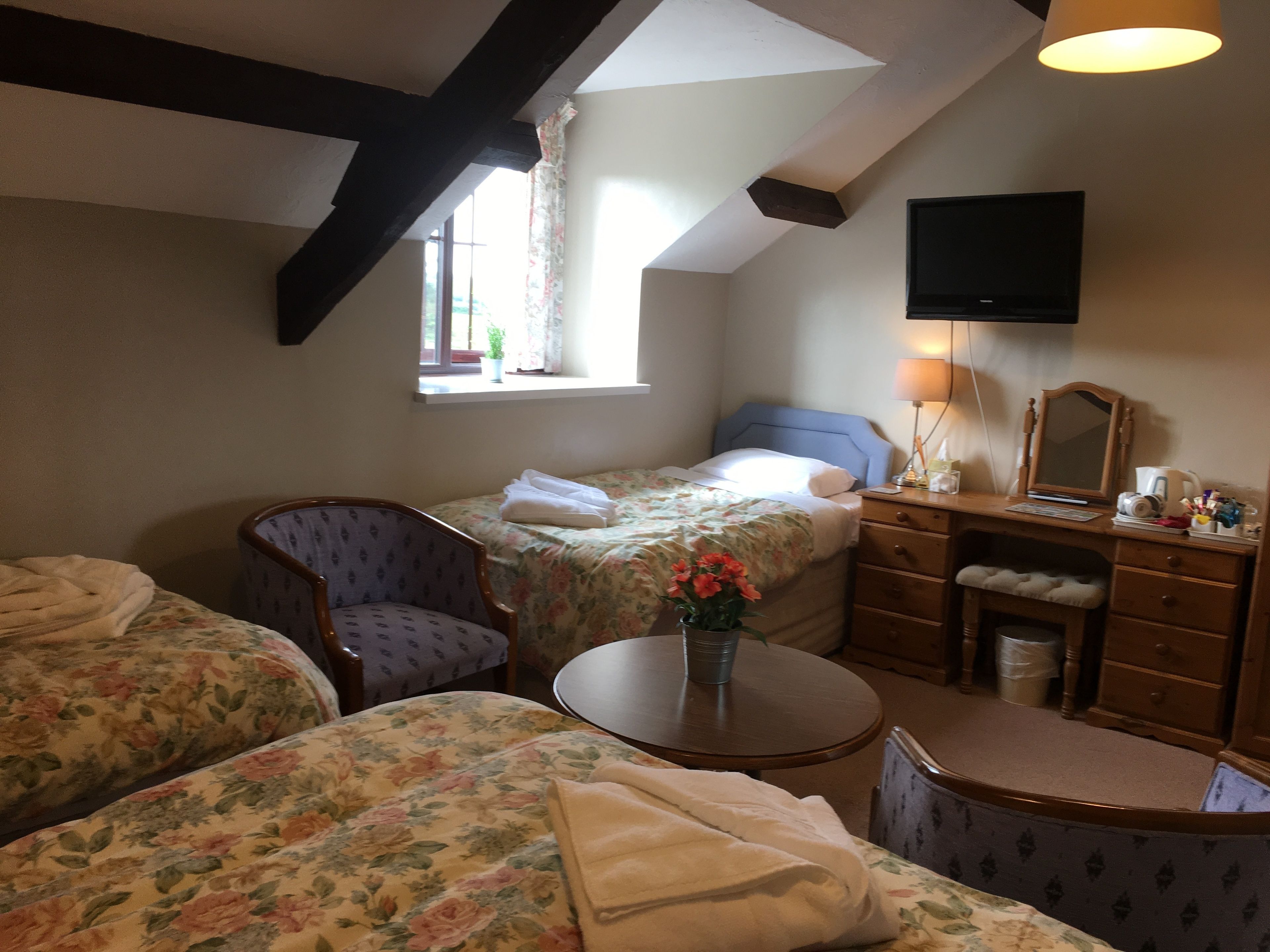 Quarto com duas camas de solteiro, cômoda de madeira, televisão e janela com cortinas.