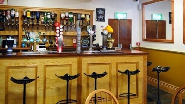 Uma área de bar com bancos de madeira, diversas garrafas de bebidas alcoólicas e um espelho na parede.