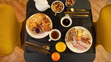 Uma bandeja de café da manhã com panquecas, croissants, presunto, ovos, suco de laranja e café.