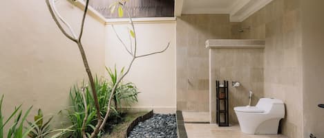 Uma casa de banho moderna com sanita independente, zona de duche e um pequeno jardim com plantas e uma árvore.