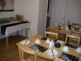 Uma sala de jantar com mesas e cadeiras de madeira, toalhas de mesa brancas e diversos utensílios de refeição.
