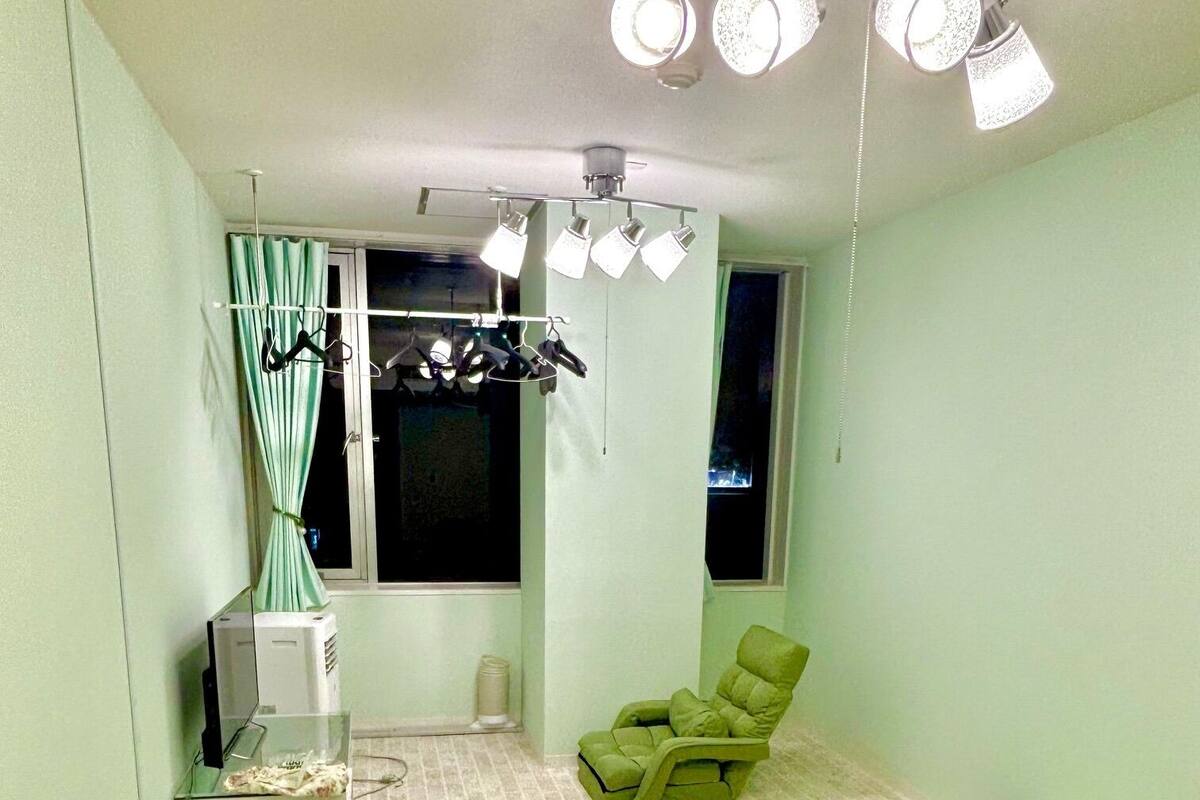Um quarto com cama, uma cadeira, uma janela e um candeeiro no teto.