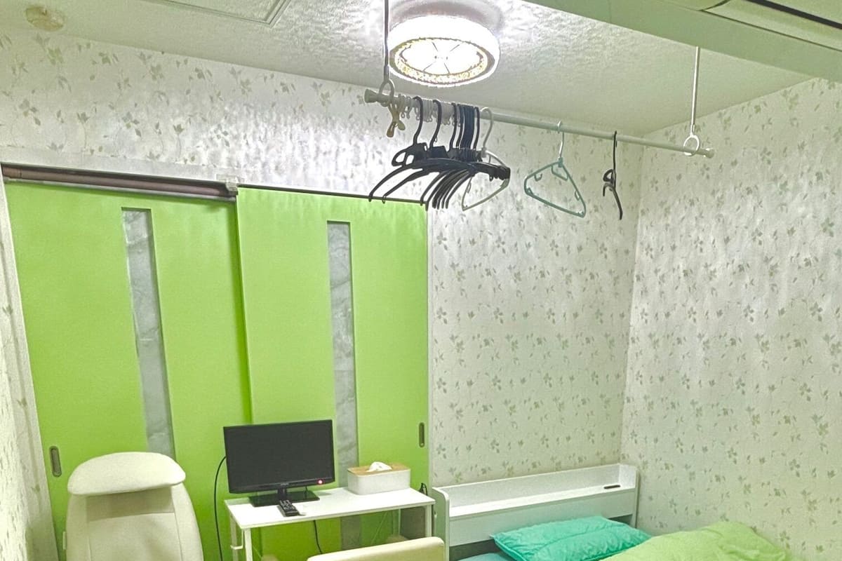 Um quarto pequeno e reservado, com uma cama, uma escrivaninha com computador, uma cadeira e um apoio para os pés.