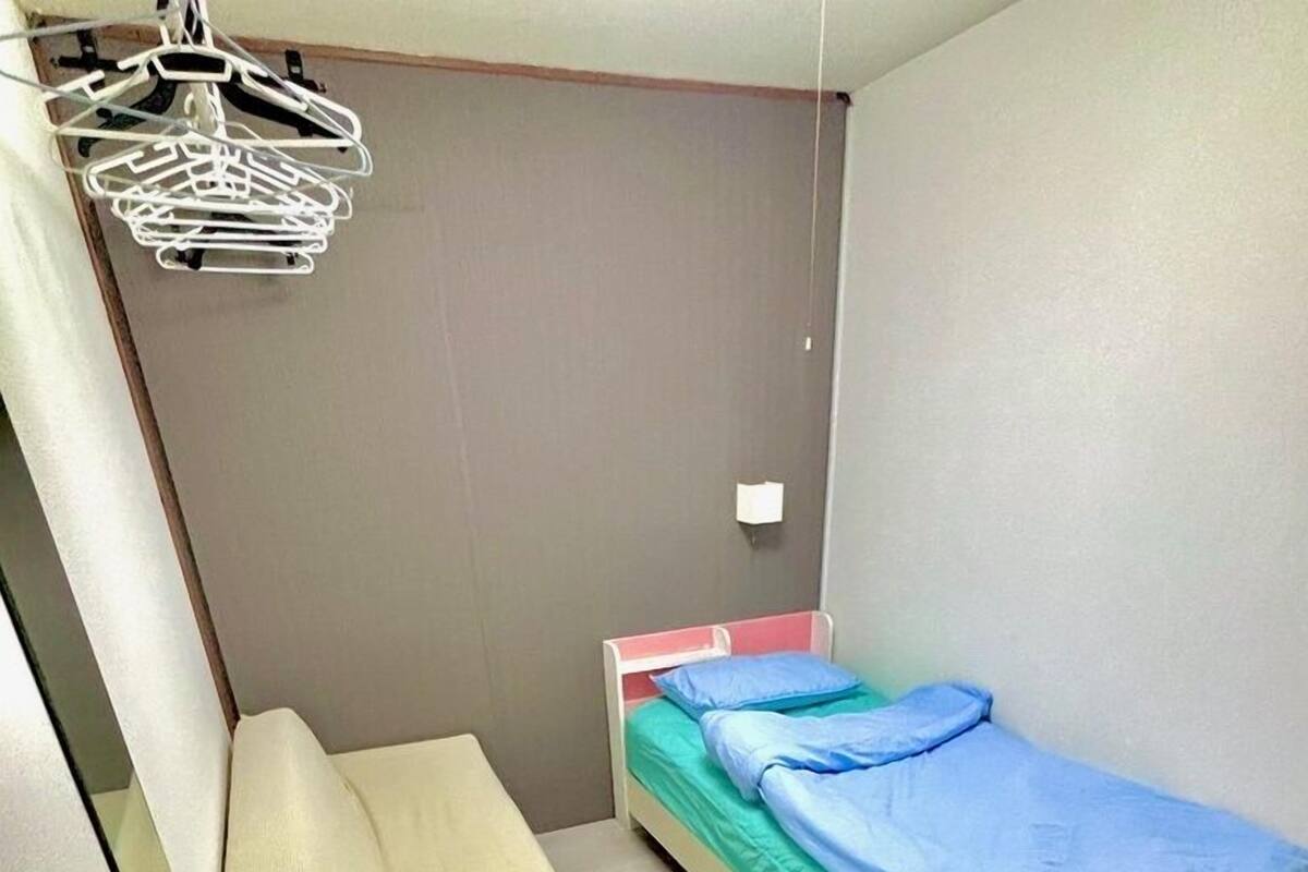 Quarto pequeno e compacto com uma cama de solteiro, um sofá e uma mesinha.