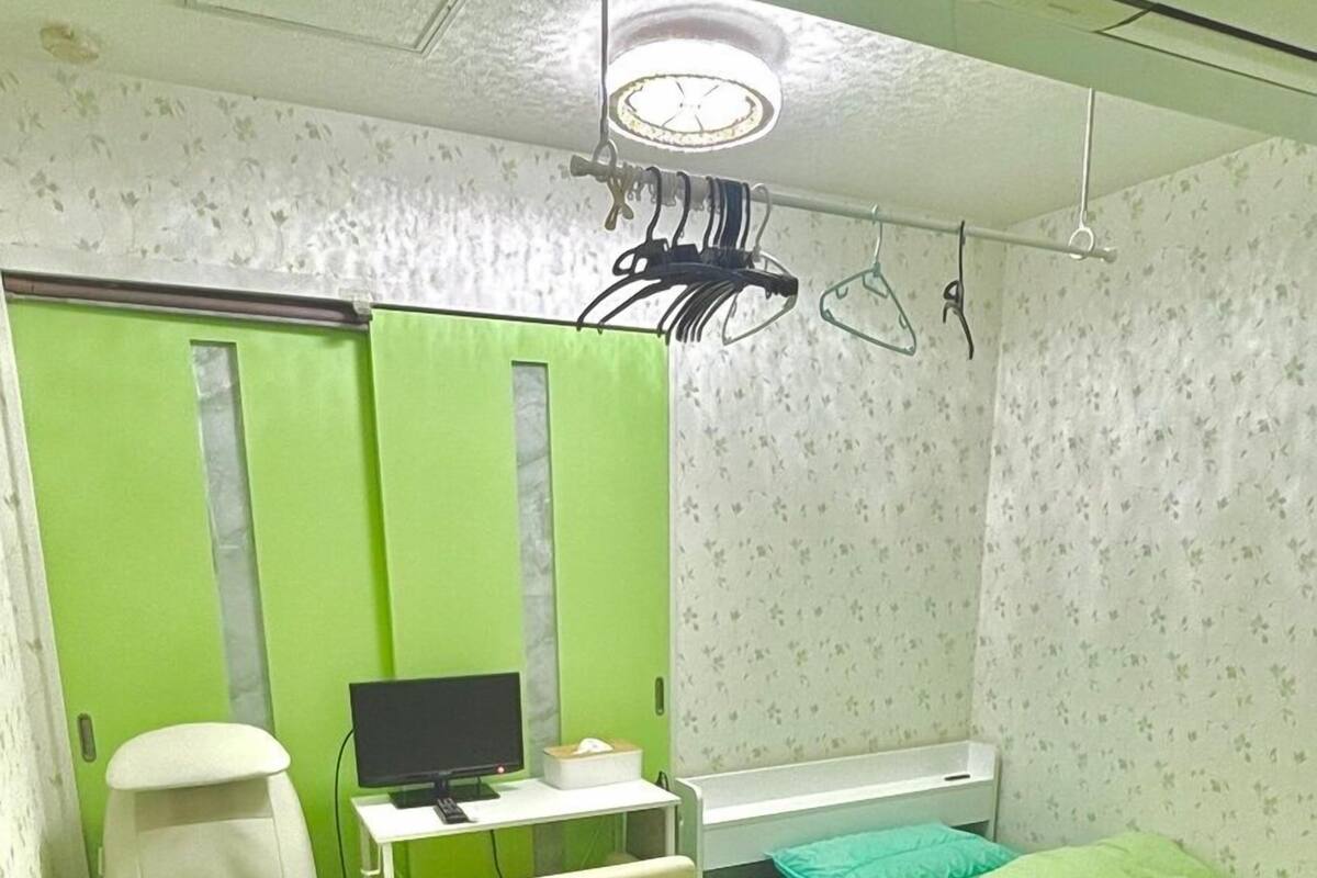 Quarto pequeno e reservado com uma cama, uma escrivaninha com um computador, uma cadeira e uma mesinha com um estojo de lenços.