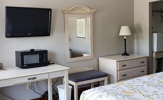 Quarto de hotel com cama, escrivaninha com micro-ondas, abajur, espelho e cómoda.