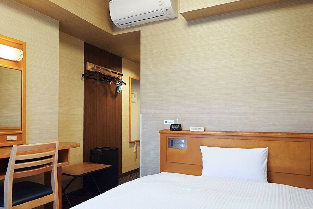 Quarto de hotel com cama, escrivaninha, cadeira, guarda-roupa e ar condicionado.