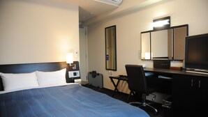 Quarto de hotel com uma cama grande, uma mesa com computador, uma cadeira e uma televisão.
