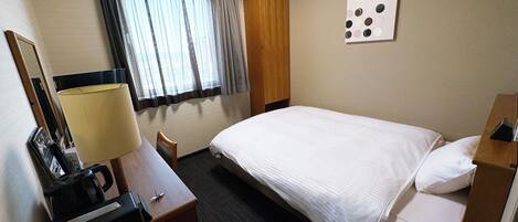 Quarto de hotel com cama, escrivaninha com luminária, cadeira, mesa pequena e obra de arte na parede.