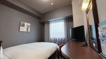 Quarto de hotel com cama, escrivaninha com televisão, espelho e janela com cortinas.