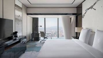 Quarto de hotel moderno com uma cama grande, escrivaninha, cadeira e televisão.