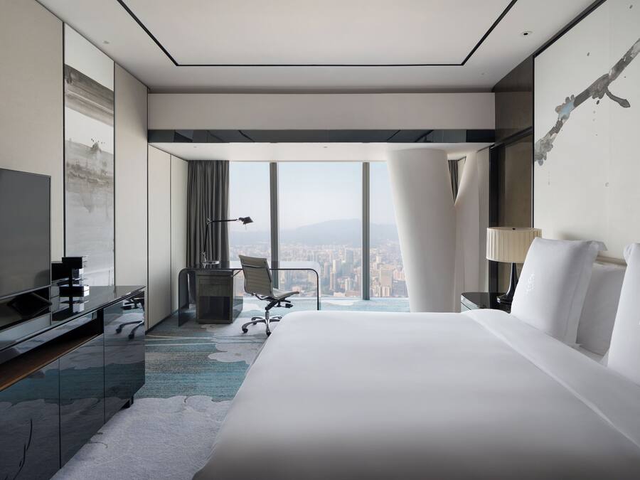 Quarto de hotel moderno com uma cama grande, escrivaninha, cadeira e televisão.