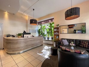 Uma área de recepção moderna com um balcão de madeira, plantas em vasos, um sofá de couro preto e um espelho grande.