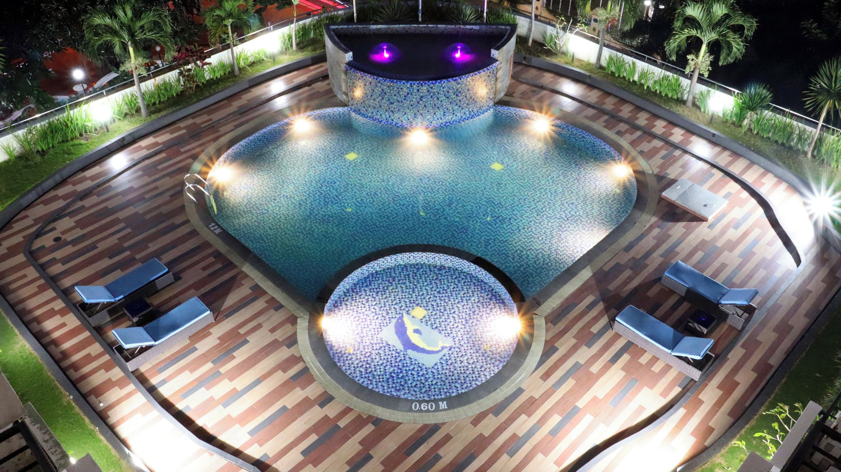 Piscina circular com fonte central, rodeada por espreguiçadeiras e um deck revestido de azulejos.