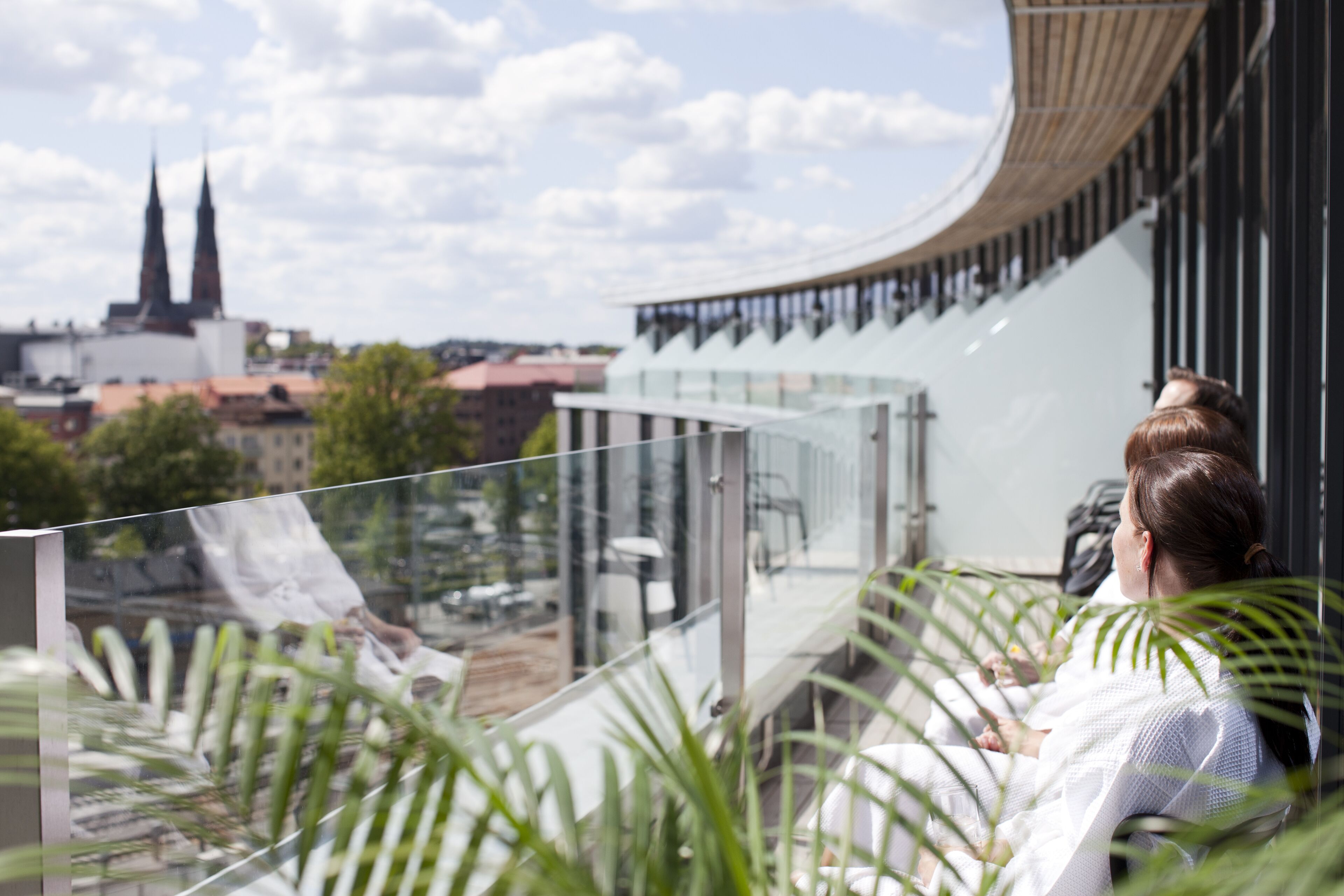 Mulher sentada numa varanda com vista para uma igreja e edifícios modernos.