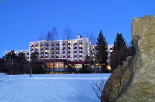 Um hotel de vários andares com fachada vermelha e branca, rodeado por neve e árvores.