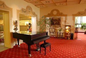 Um piano de cauda em um quarto com carpete estampado em vermelho, um espelho grande e um lustre.