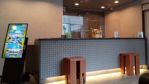 Uma área de recepção com balcão revestido de azulejos, um painel de menu digital e dois bancos de madeira.