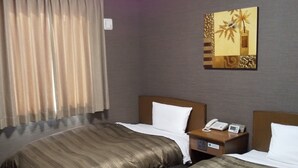 Quarto de hotel com duas camas, uma mesa de cabeceira com telefone e relógio, um quadro na parede e uma janela com cortinas.