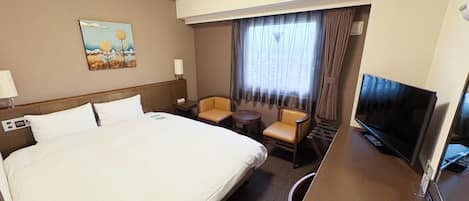 Quarto de hotel com uma cama grande, uma escrivaninha com televisão, uma cadeira e uma pequena mesa.