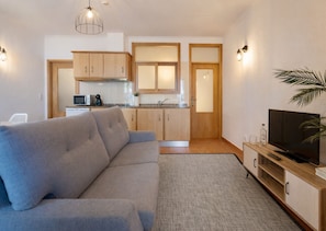 Uma sala de estar moderna com um sofá cinza, uma televisão e uma área de cozinha com armários de madeira e micro-ondas.