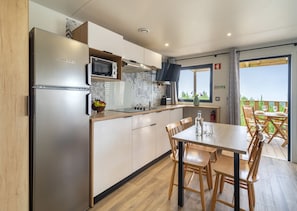 Uma cozinha moderna com geladeira, micro-ondas e fogão, uma mesa de jantar com cadeiras, e vista para o verde lá fora.
