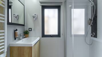 Casa de banho moderna com lavatório branco, espelho, janela, chuveiro e porta-toalhas.
